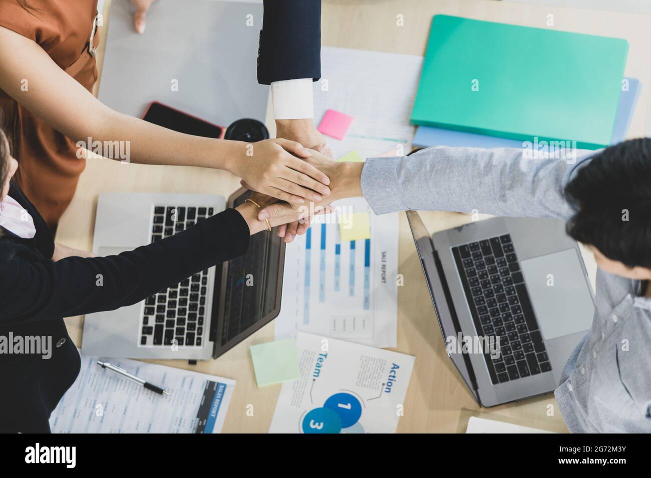 A Group of four businesspeople working around the desk and stack their ...
