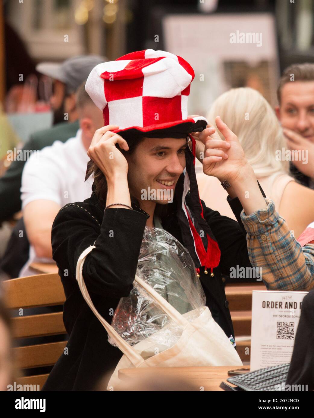A man tries on his England hat while dining in Soho, central London ...