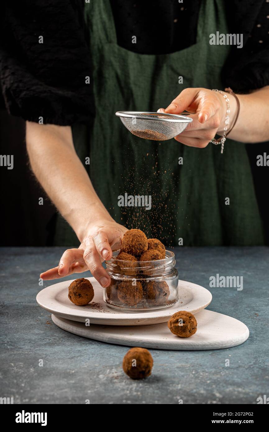 A woman sprinkle the chocolate balls with cocoa powder. Healthy kitchen ...