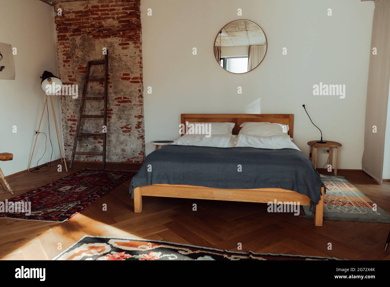 Interior of a loft-style bedroom with a wooden bed and colorful carpets ...