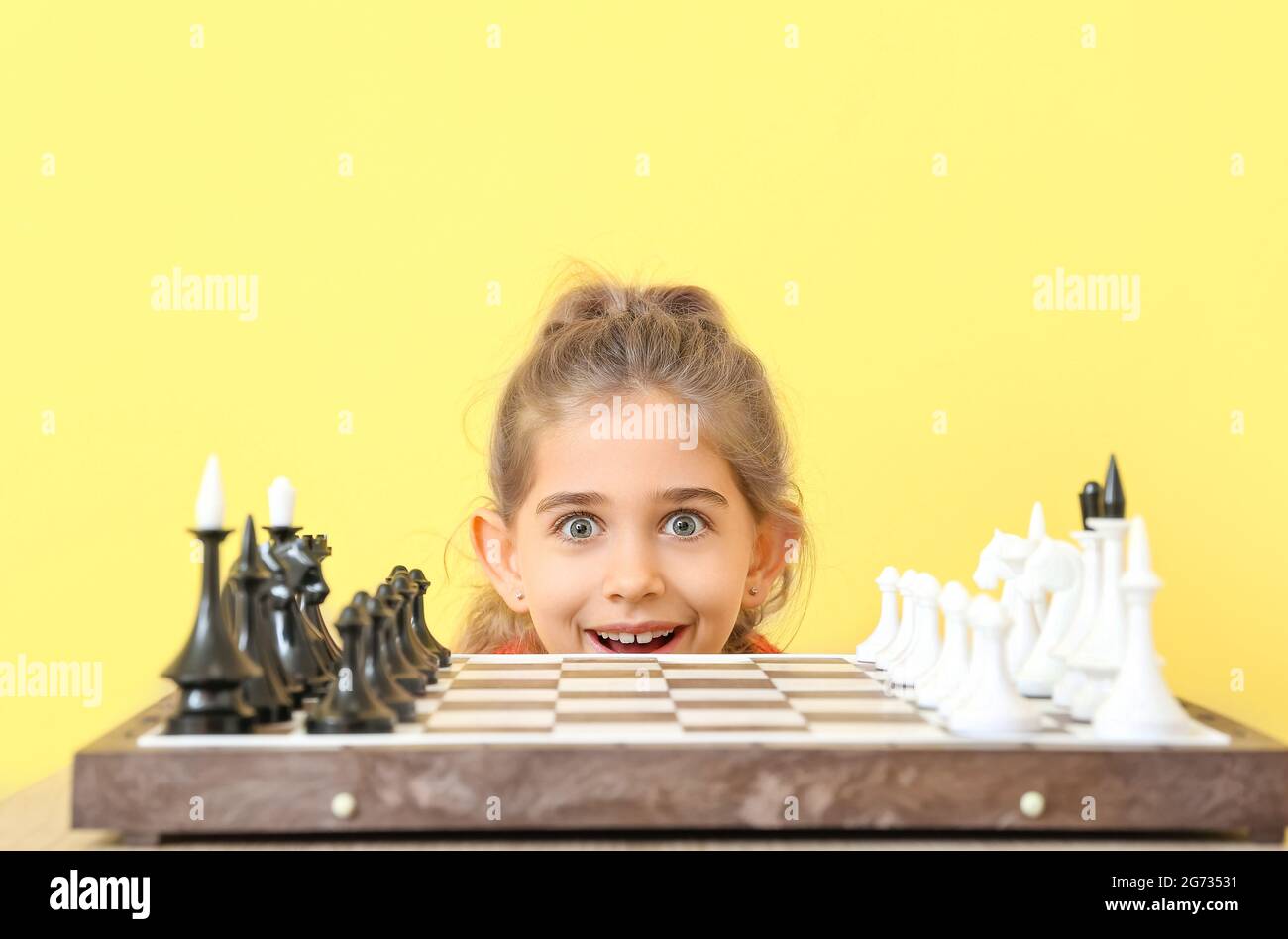 Cute little girl playing chess on color background Stock Photo - Alamy