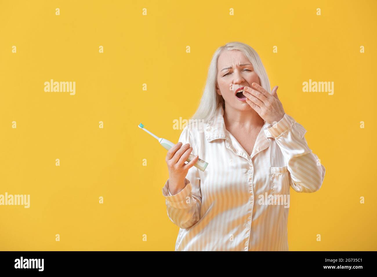 Sleepy mature woman brushing teeth on color background Stock Photo - Alamy