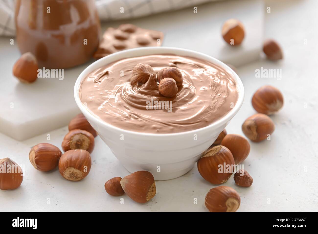 Bowl with tasty chocolate paste and hazelnuts on light background Stock ...