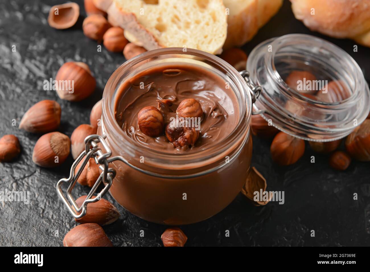 Jar with tasty chocolate paste and hazelnuts on dark background Stock ...