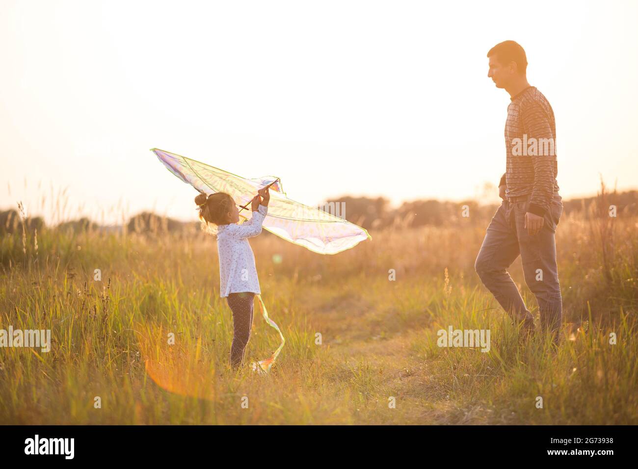 Dad helps his daughter to fly a kite in a field in the summer at sunset ...