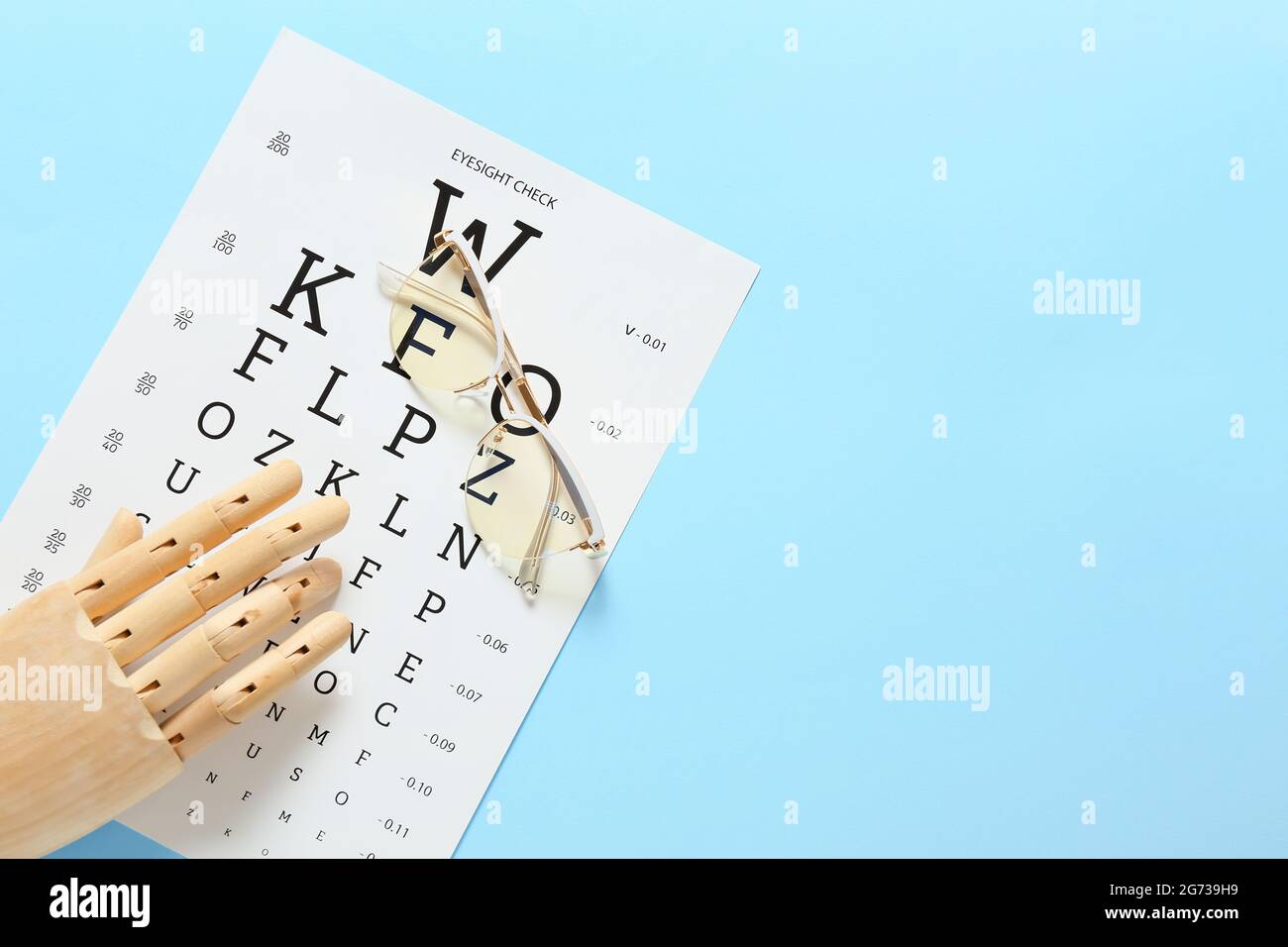Eyeglasses with wooden hand and eye test chart on color background ...
