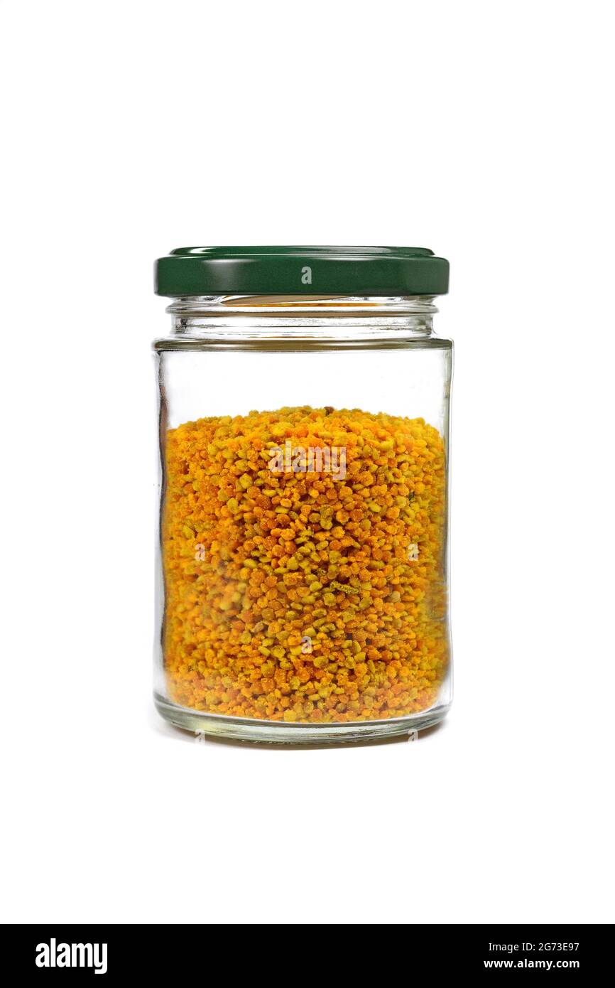 bee pollen in a transparent glass jar spilled on a white background ...