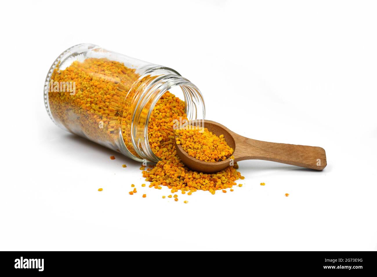 bee pollen in a transparent glass jar and wooden spoon spilled on a ...