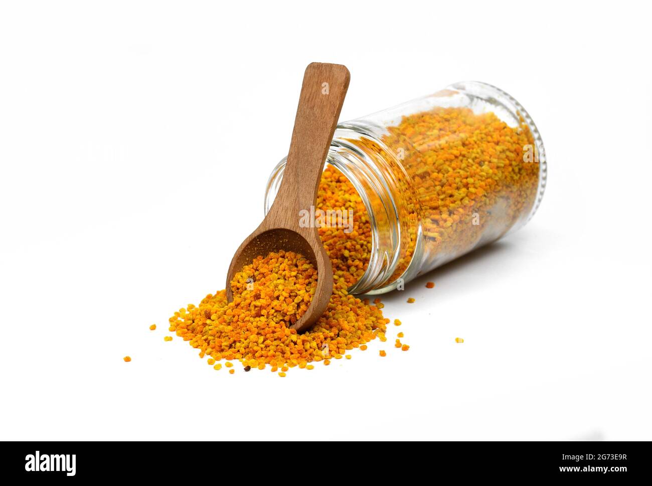 bee pollen in a transparent glass jar and wooden spoon spilled on a ...