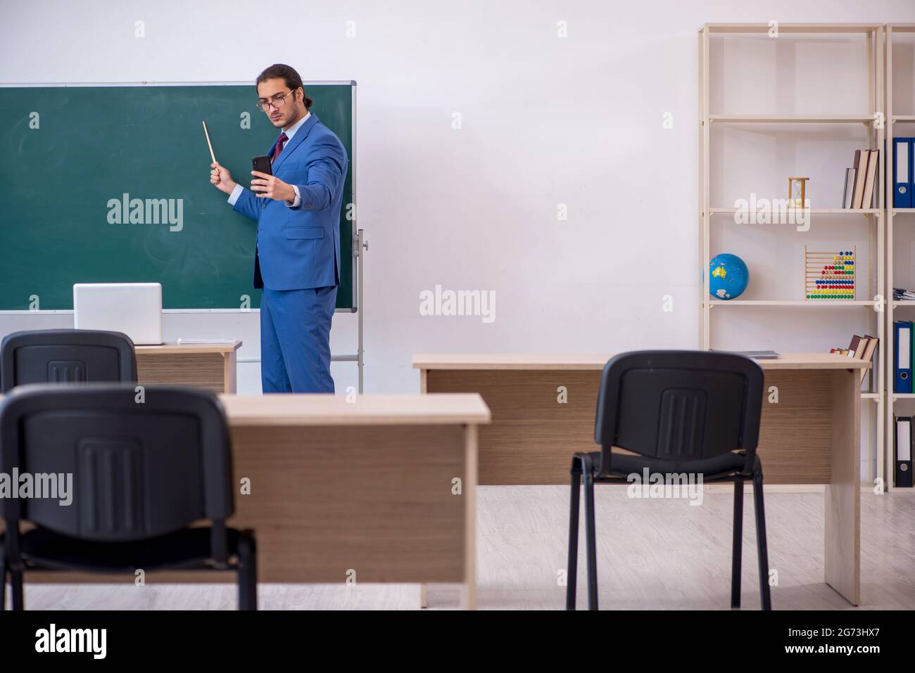 Young teacher in suit in front of green board Stock Photo - Alamy