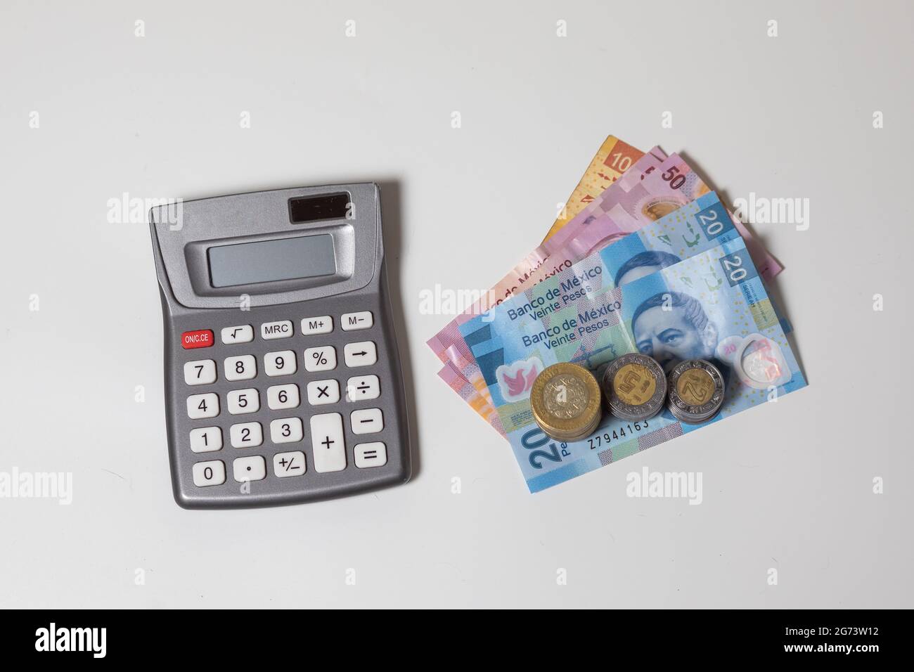 A stack of paper money and coins and a calculator on a light gray ...