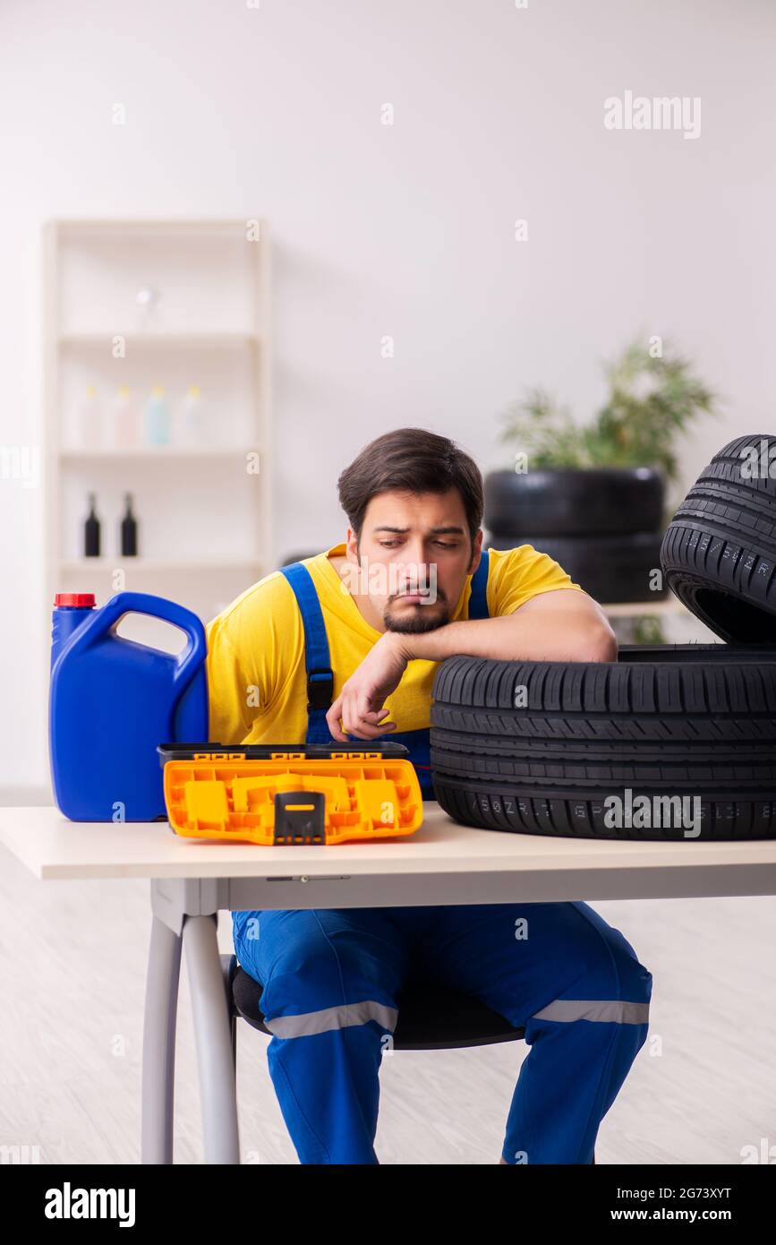 Young garage worker with tyre at workshop Stock Photo - Alamy