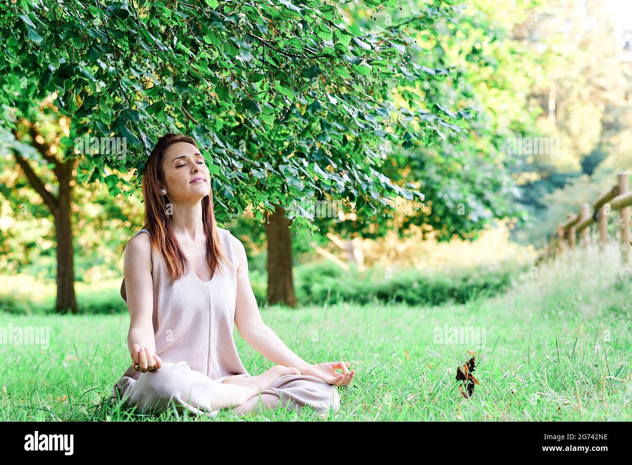 young adult woman in lotus position doing yoga in a park sitting on the ...