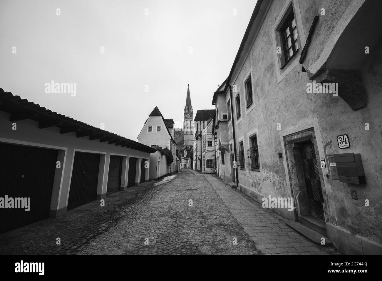 A grayscale shot of a long alley through stone residential buildings ...