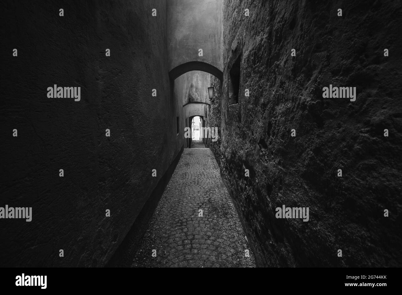 A grayscale shot of a narrow long alley through high stone buildings ...