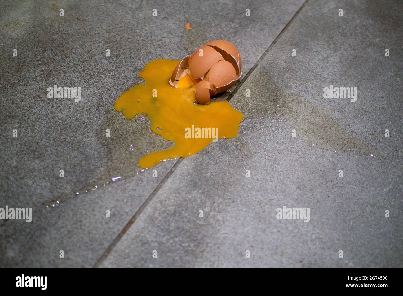 Smashed egg on grey tile floor with cracked and broken shell, egg yolk ...