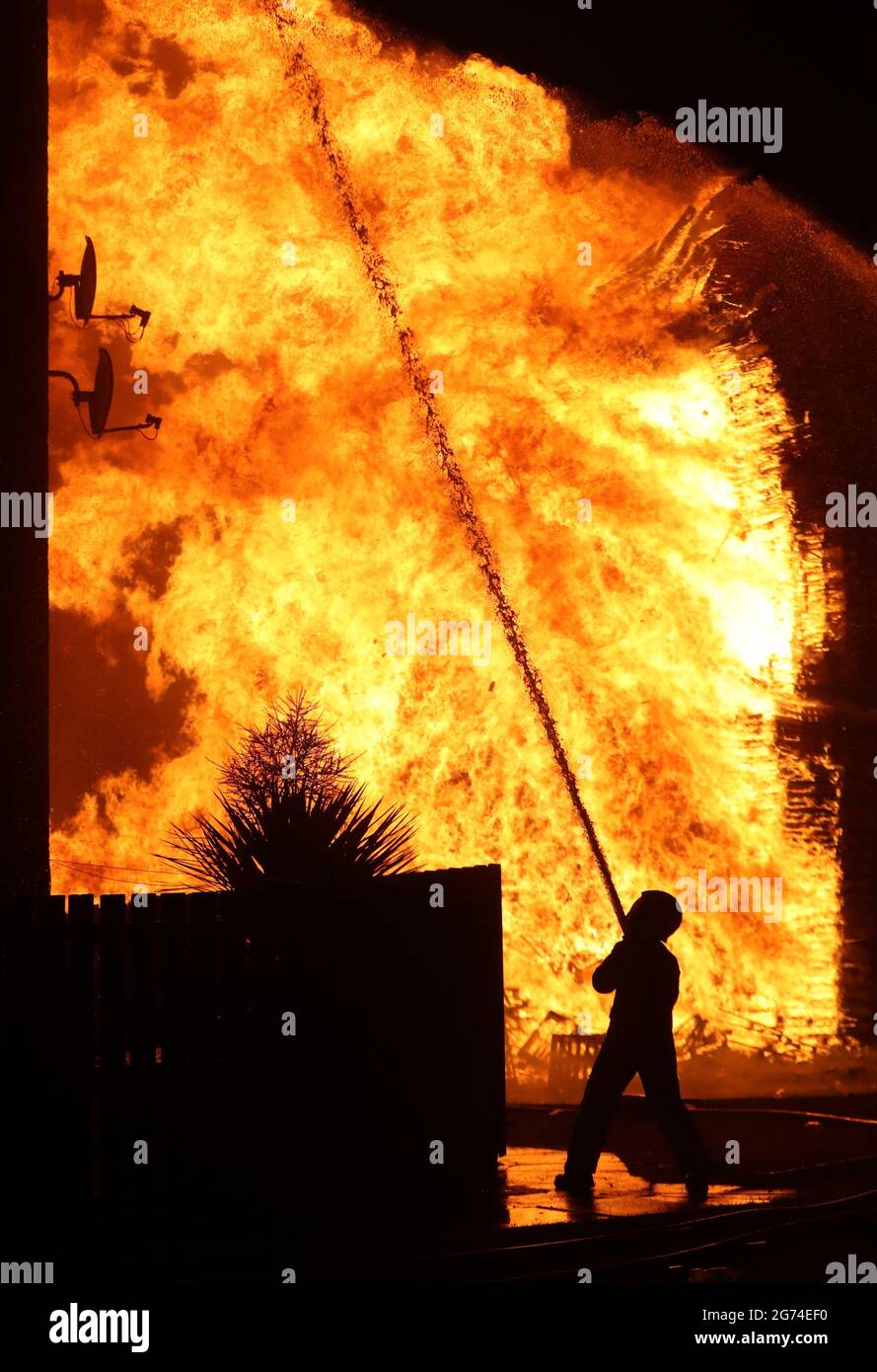 Fire fighters dampen down nearby properties as a huge bonfire in the ...