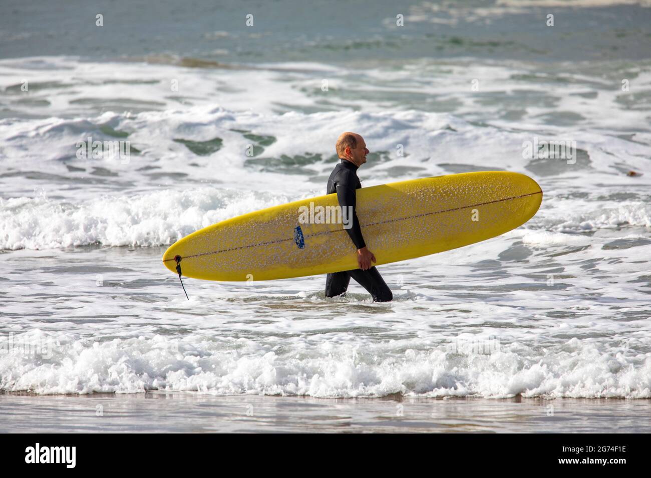 Australian middle aged surfer in wetsuit carries his surfboard in the ...