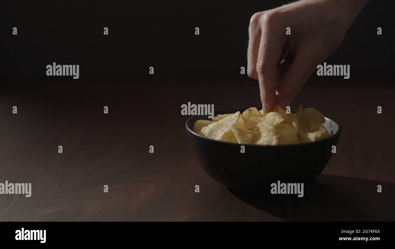 man take organic potato chips from black bowl on walnut table wide ...