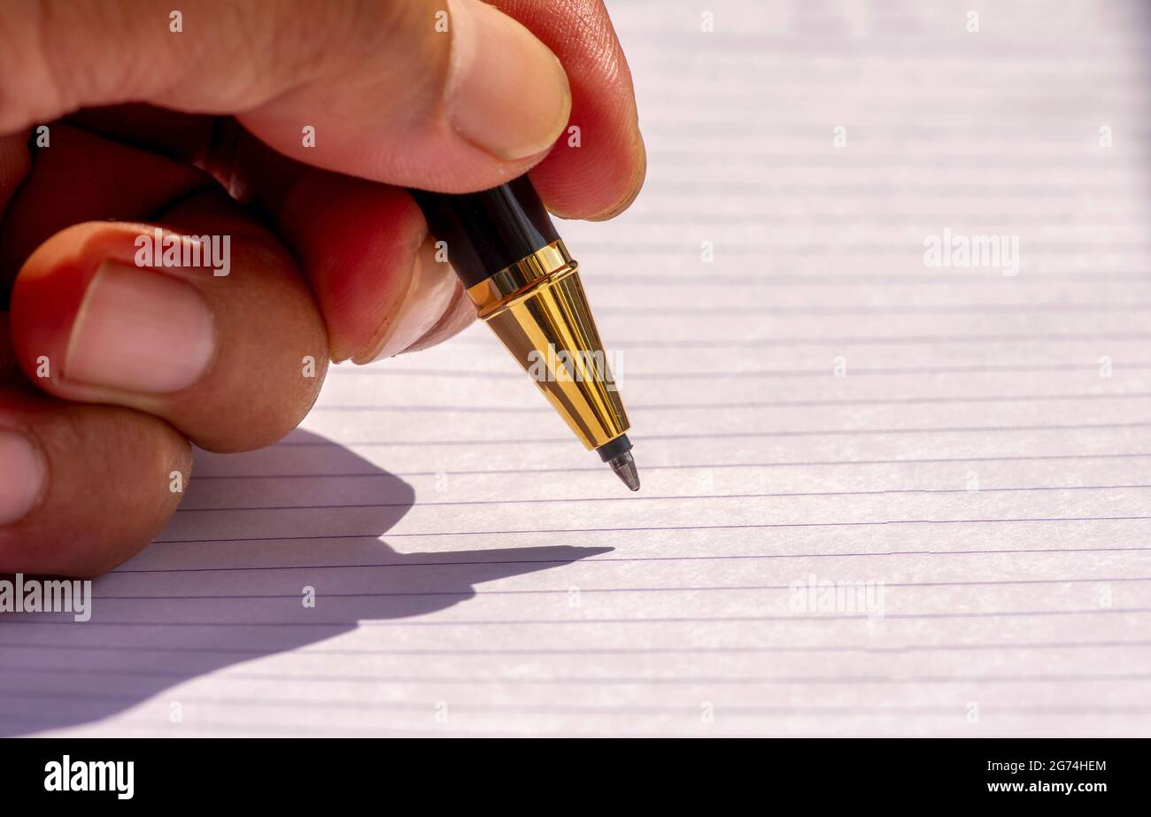 Left handed writing with a gold pen, in shallow focus on white lined ...