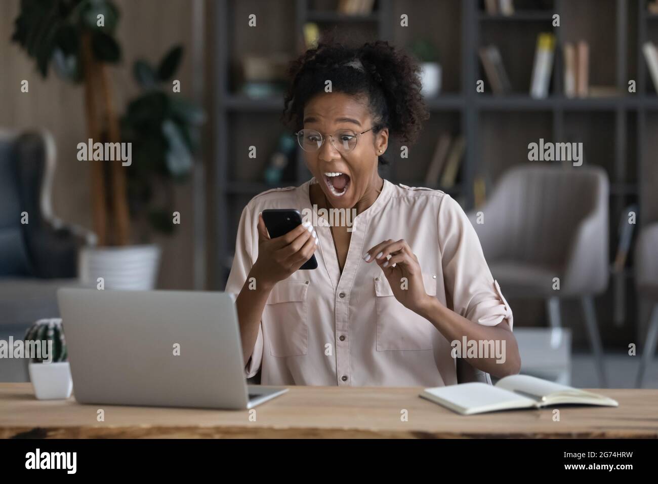 Overjoyed Surprised African American Woman In Glasses Using Smartphone
