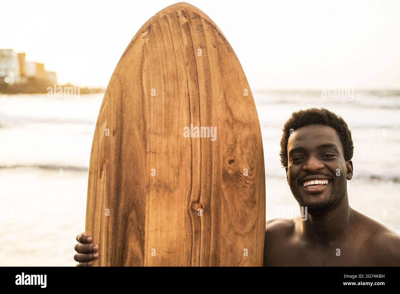 Black surfer man holding vintage surf board on the beach at sunset ...