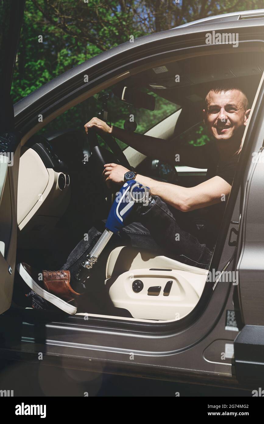 a man on a prosthetic leg sits in a car. Dressed in black jeans and a T ...
