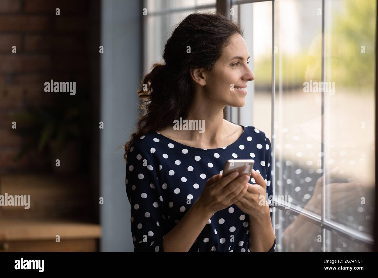 Happy pensive user with cellphone looking away out window Stock Photo ...