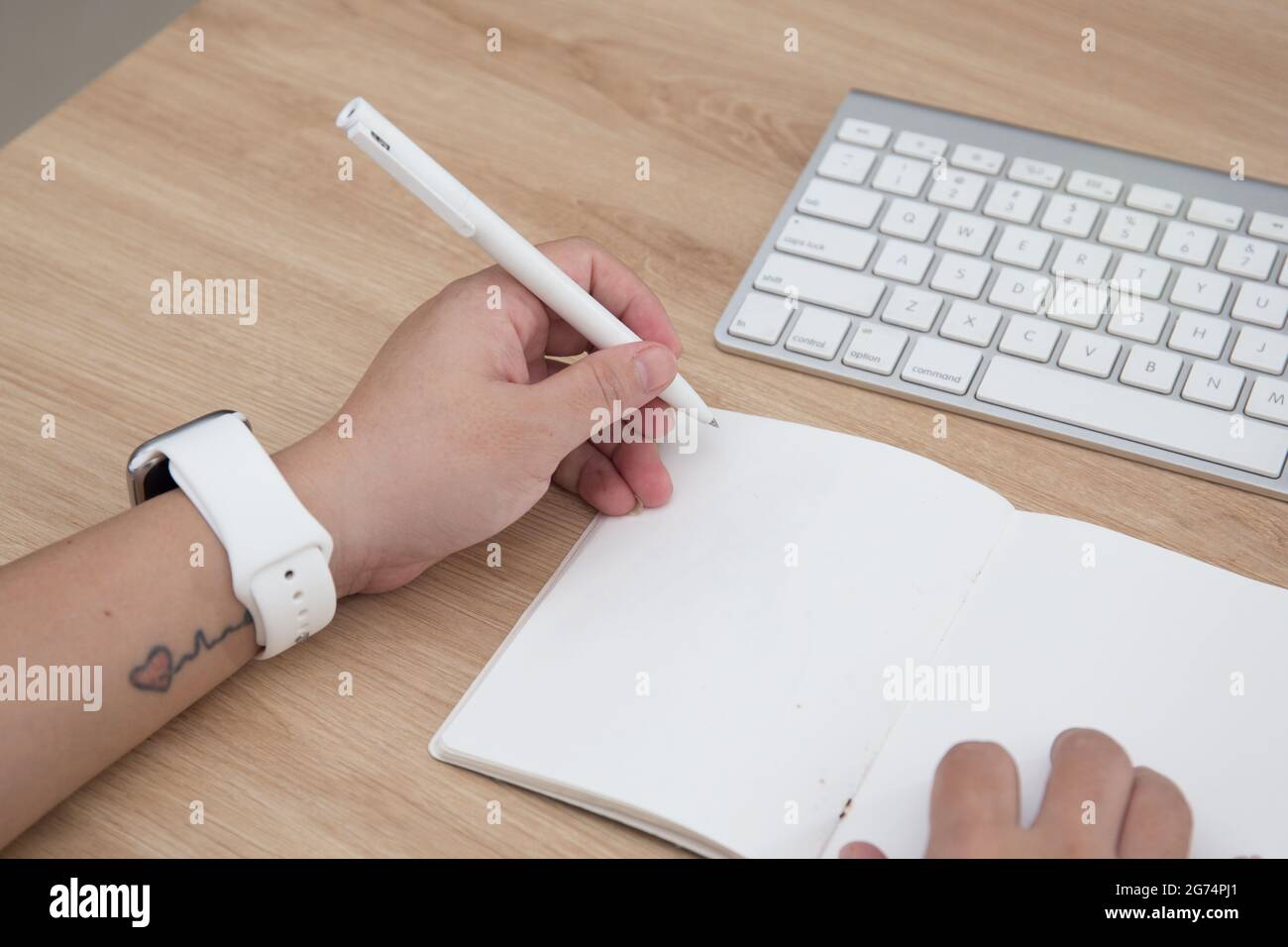 A high angle shot of female hands writing in notebook and a keyboard on ...