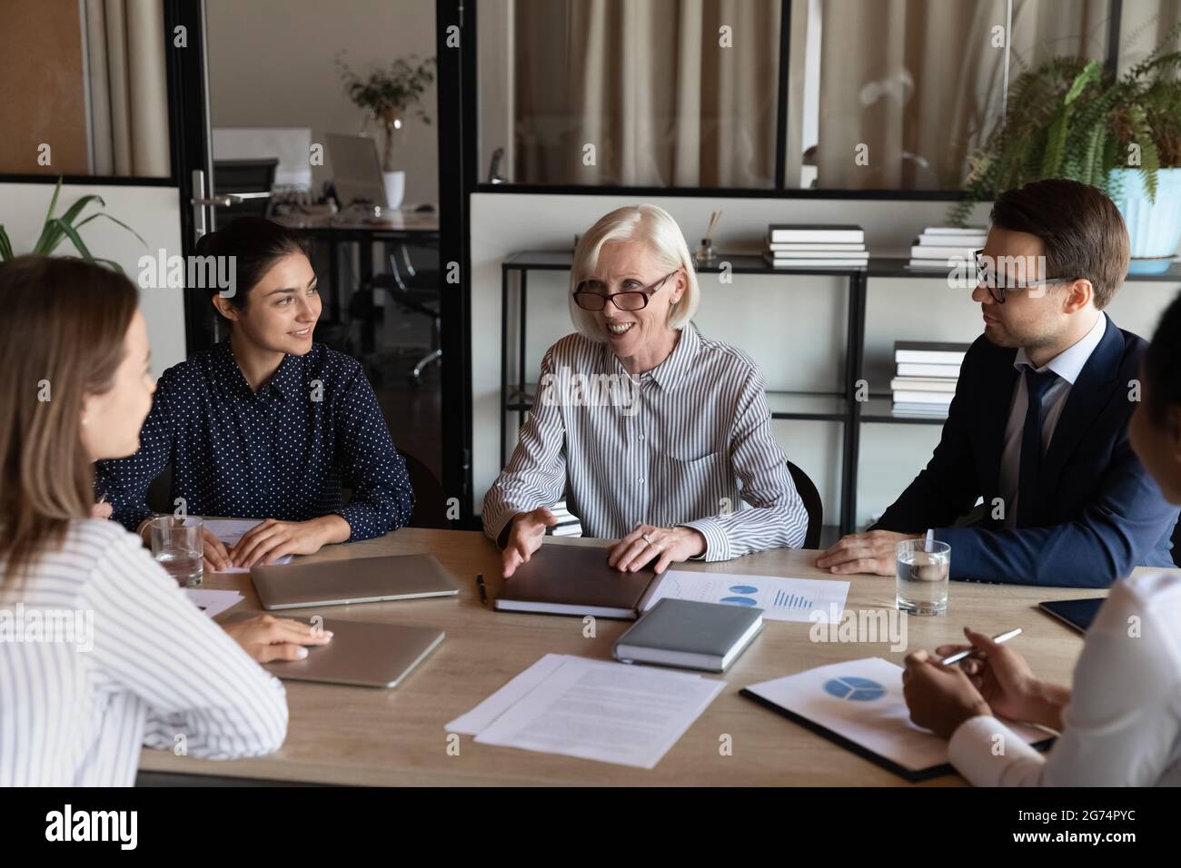 Happy mature female business leader talking to team, giving ...