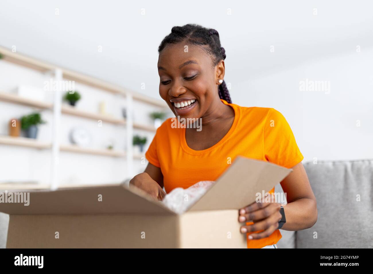 Portrait of curious black woman receiving package, unboxing cardboard ...