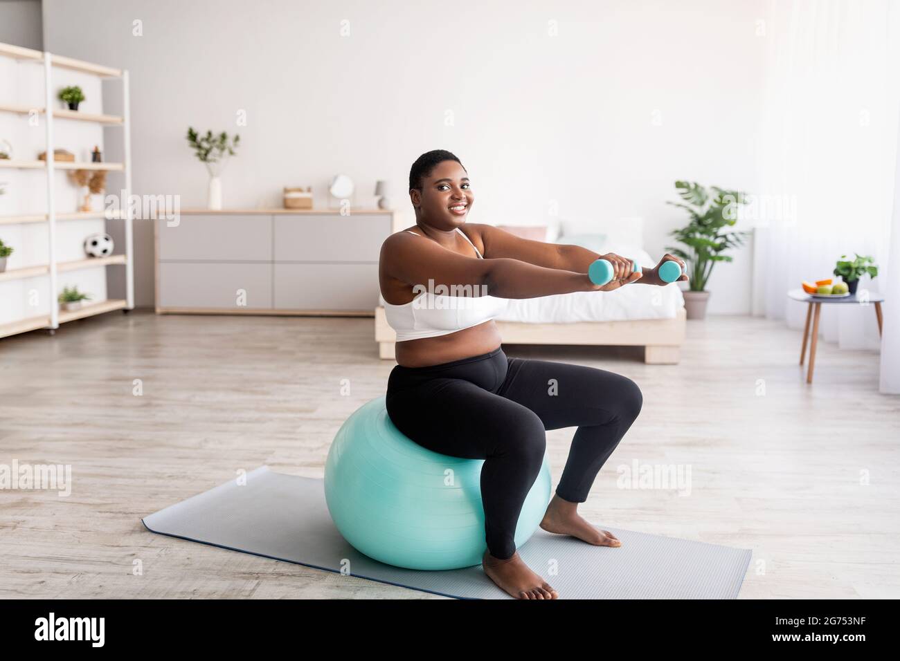 Plus size black woman working out with dumbbells on fitness ball at ...