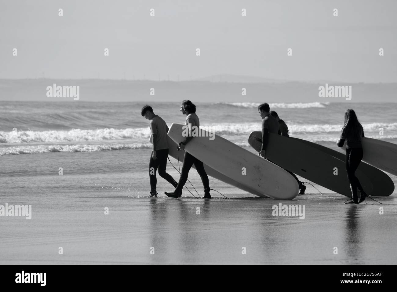 Surfers of all ages carry surfboards to the water's edge of Llangennith ...