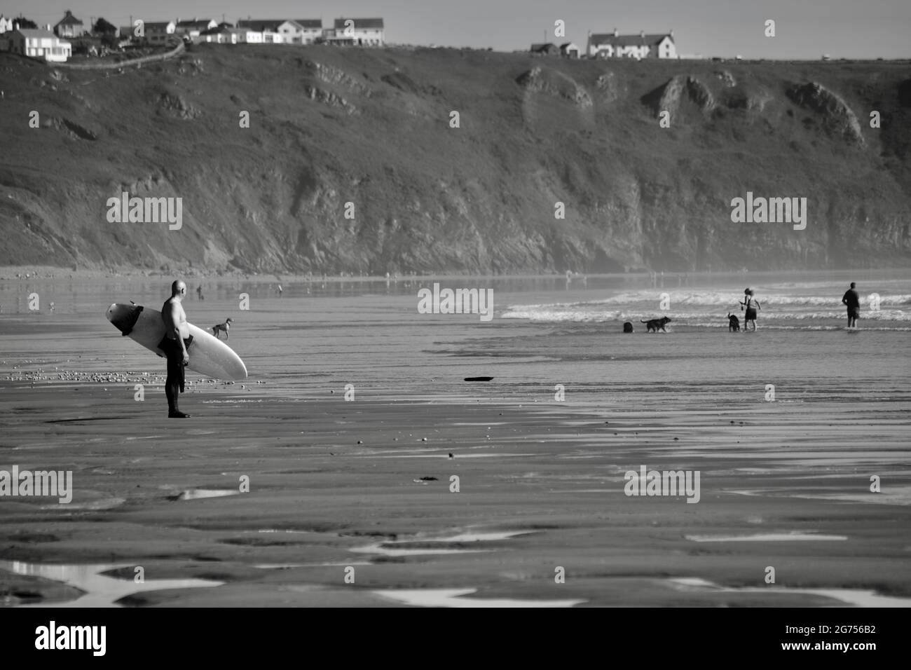 Surfers of all ages carry surfboards to the water's edge of Llangennith ...