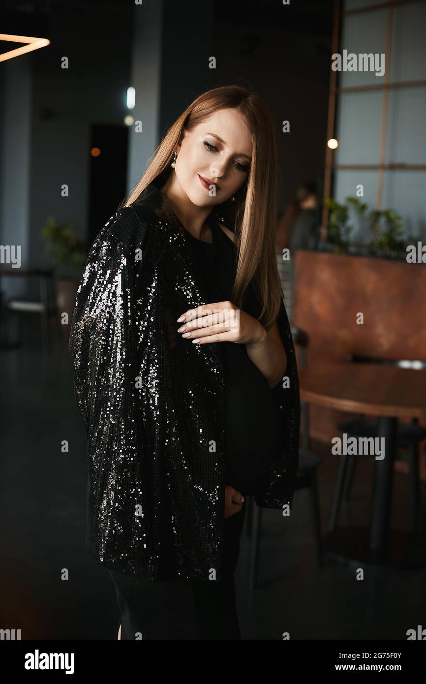 A young pregnant woman with bright makeup in a trendy black dress and ...