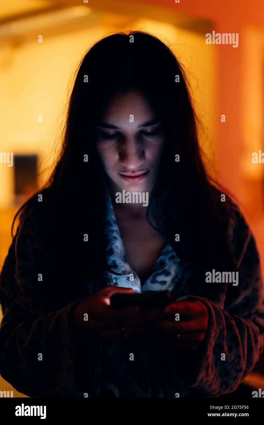 A young woman in dressing gown using a phone at night at home Stock ...