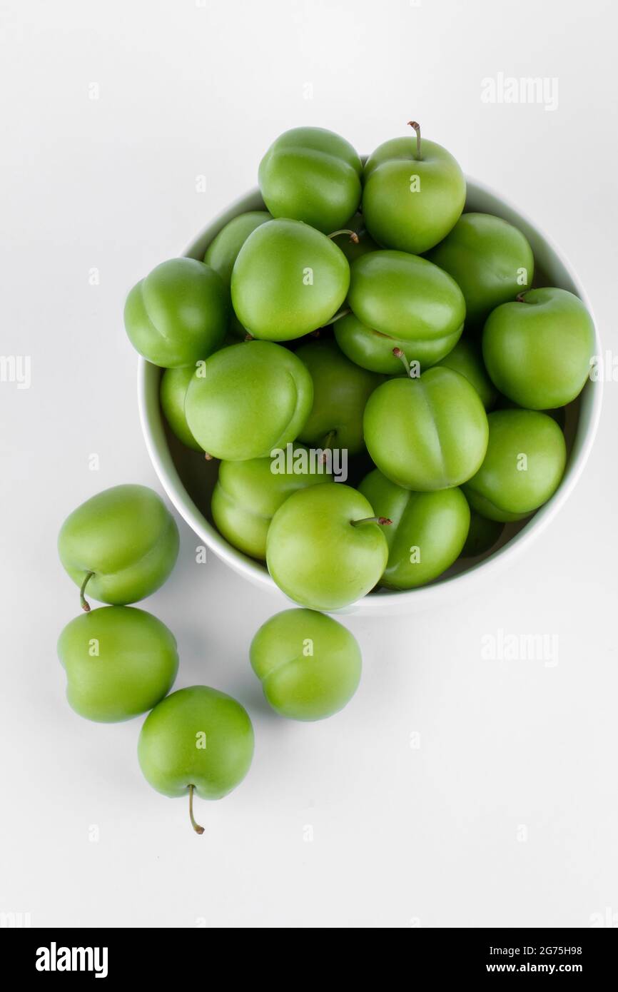 A vertical top view of a heap of sour green plums in a bowl on a plain ...