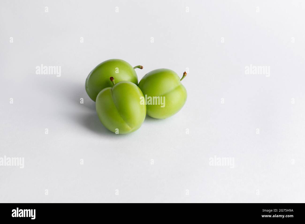 A triplet of fresh, sour green plums isolated on a bright white ...