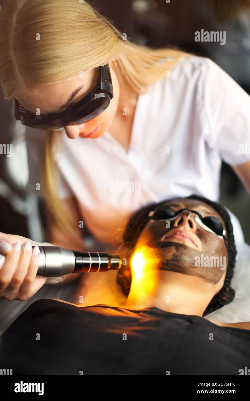 Beautician holding beauty laser near woman face covered with carbon ...