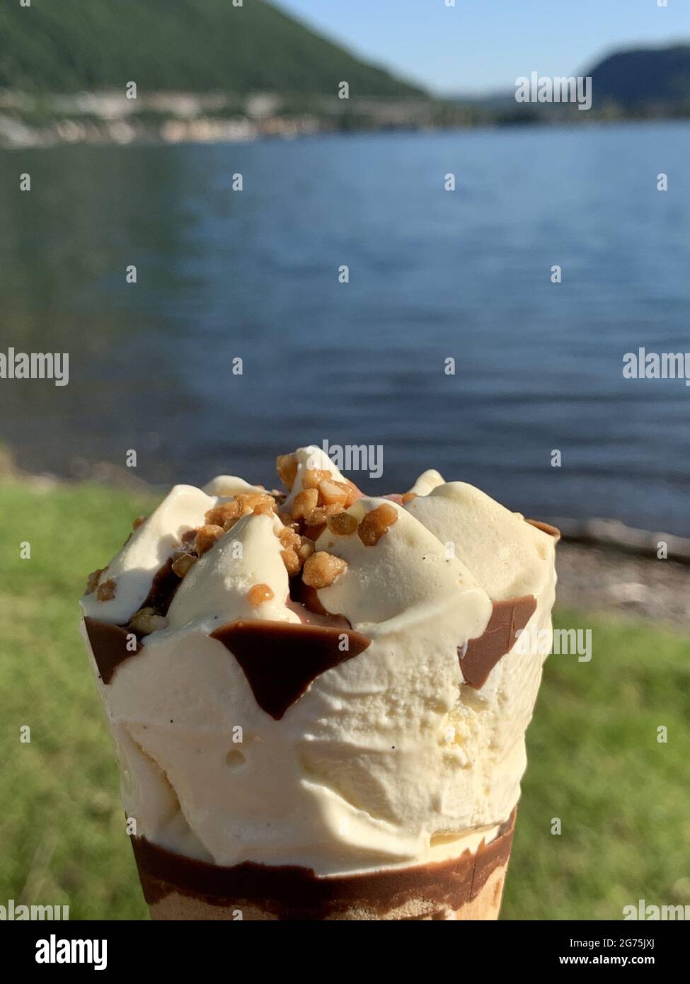 A vanilla ice cream with chocolate topping and nuts by the lake on a ...
