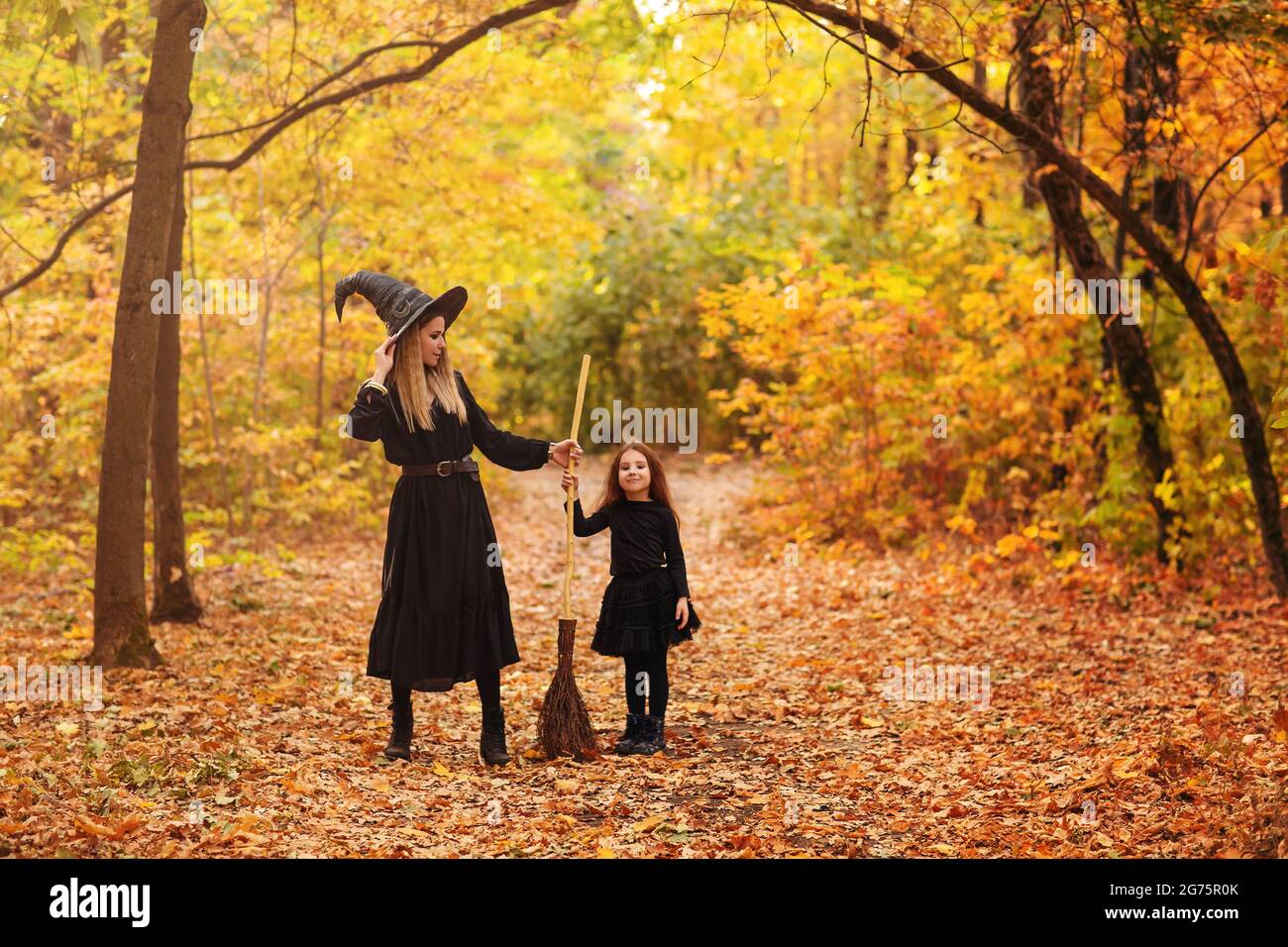 Full body woman and girl in witch costumes sweeping withered leaves ...