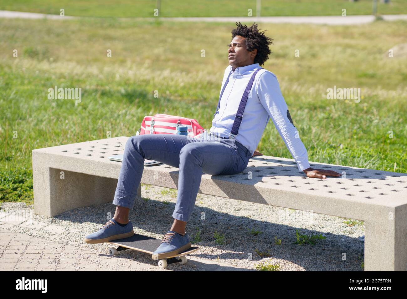 Black man with afro hair taking a coffee break sitting on a park bench ...