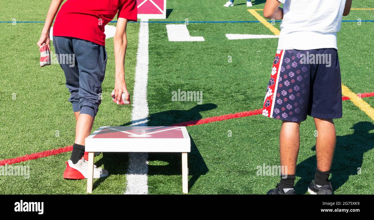 Rear view of two boys playing cornhole bean bag toss game on a turf ...