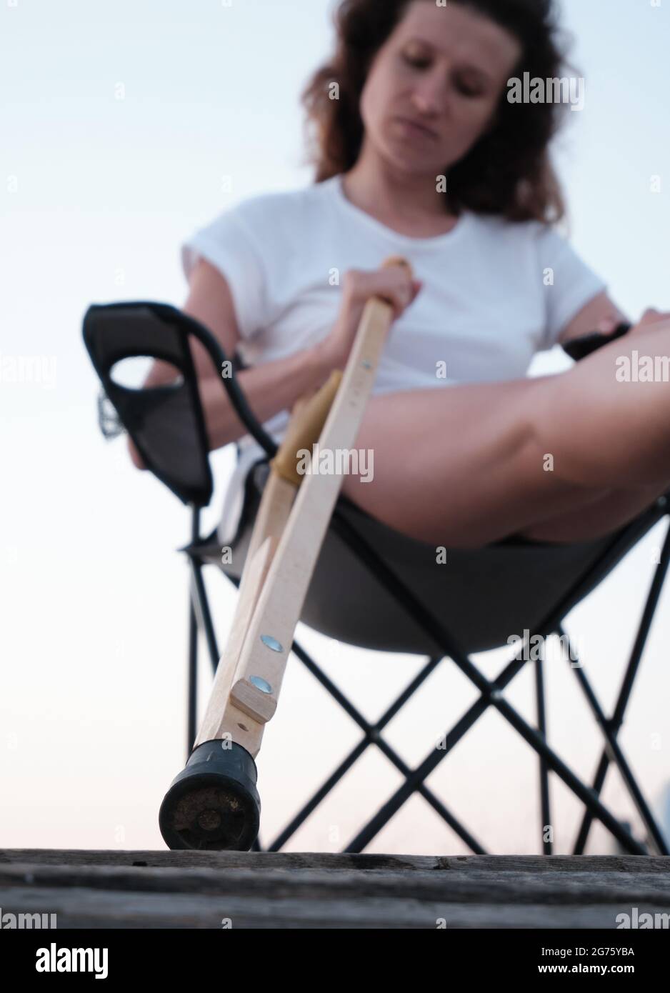 Woman with broken in cast is sitting on chair in nature. Leg injury ...