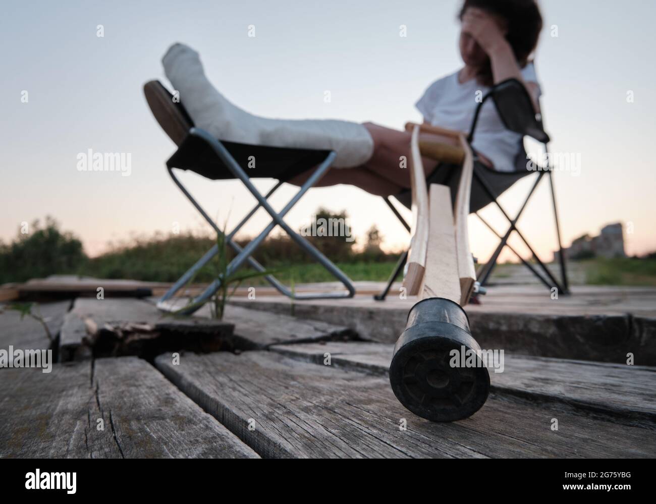 Woman with broken in cast is sitting on chair in nature. Leg injury ...
