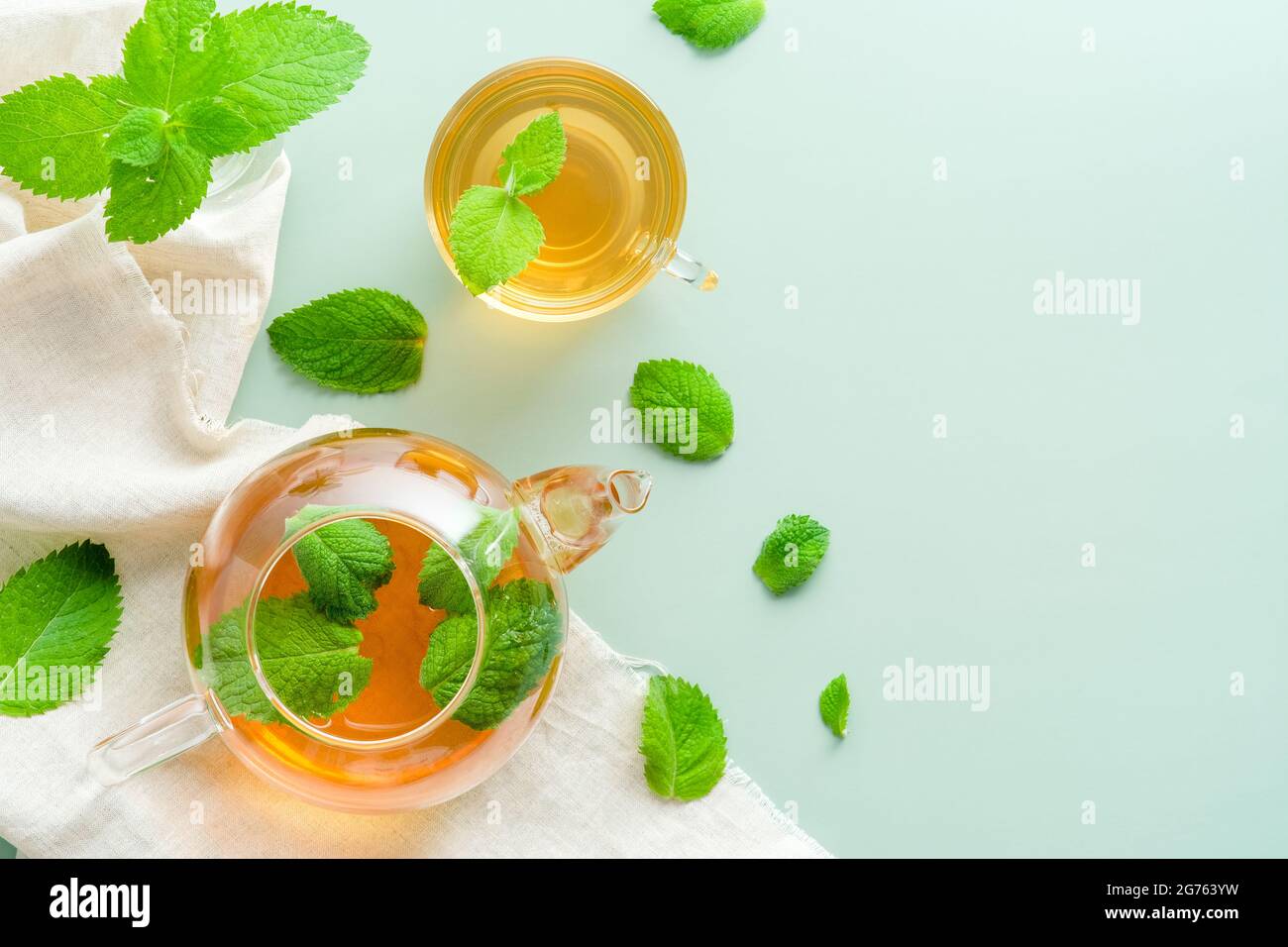 Fresh mint tea in cup and pot on green background with mint leaves ...