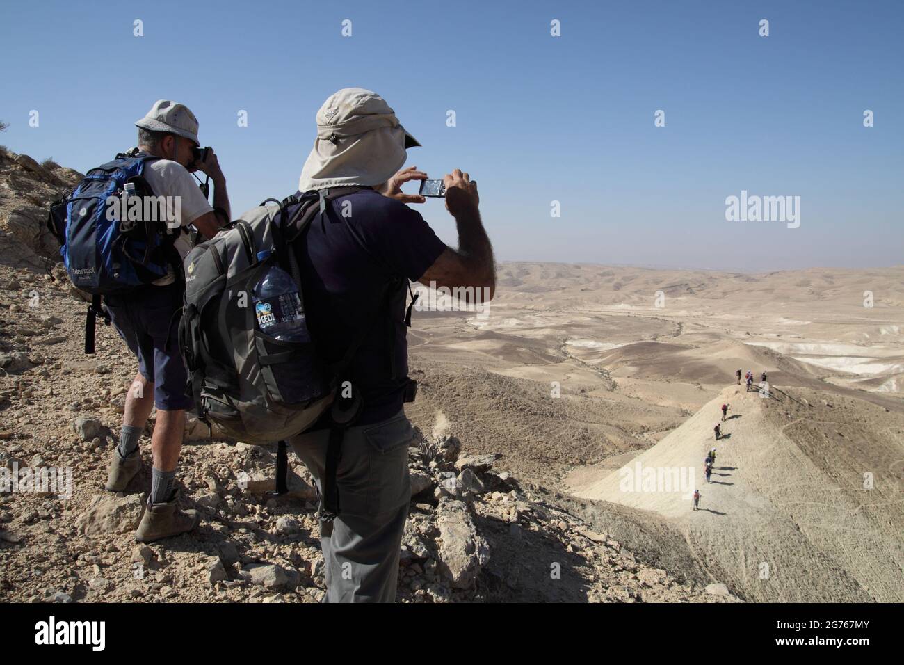 Hikers, senior adults, stand on a hill photographing their friends hike ...