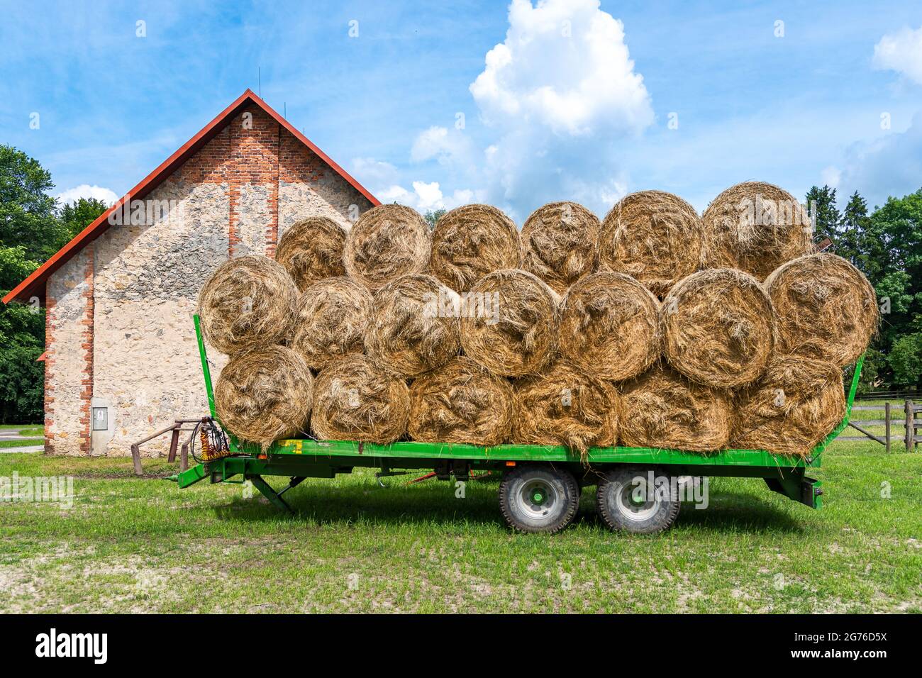 Green trailer filled with hay bales parked in the front of brick barn ...