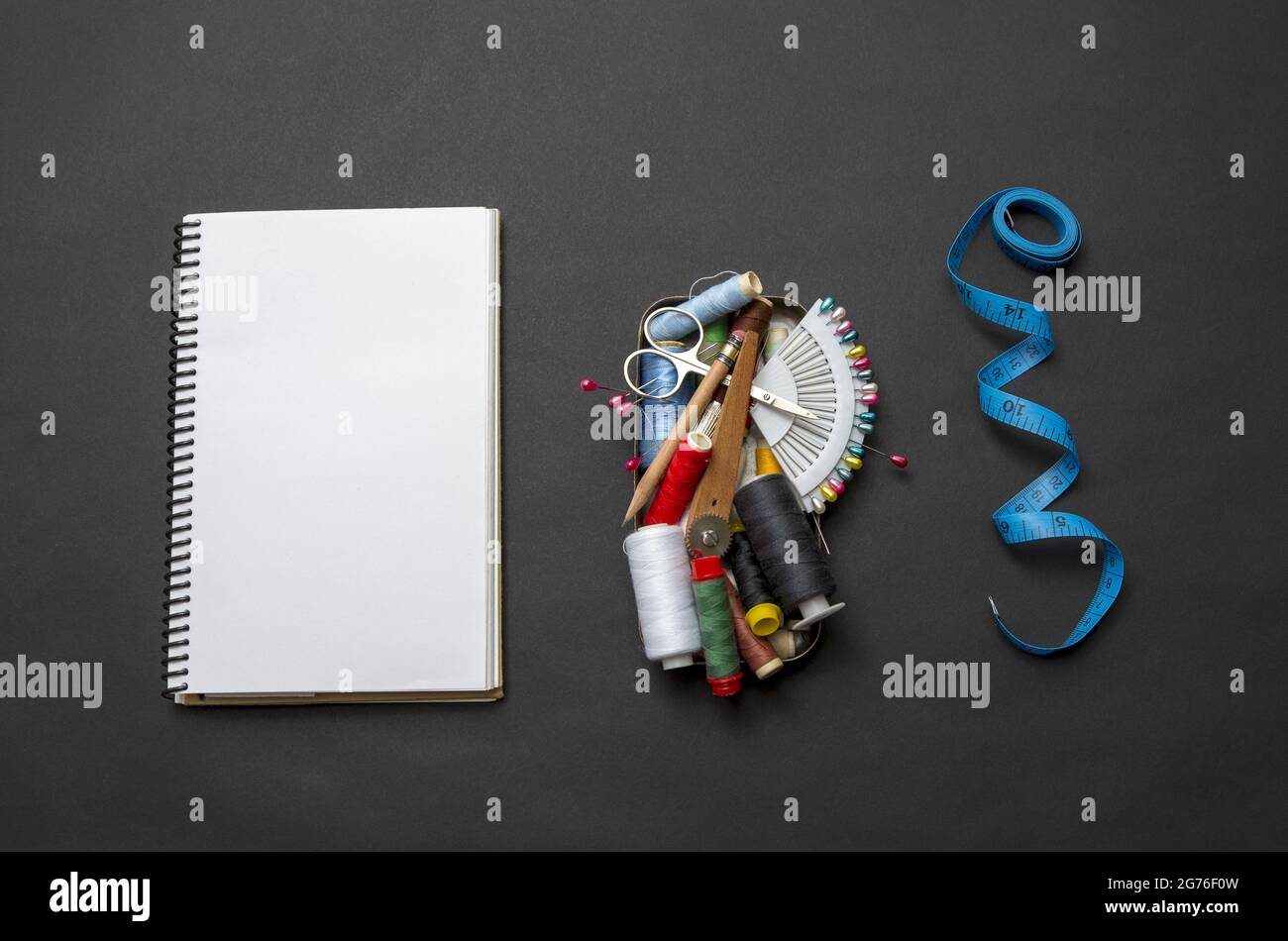 A top view of a white notebook, threads, and scissors over a black ...