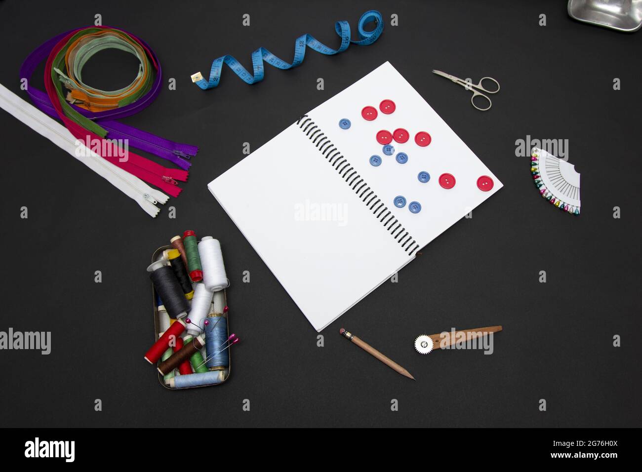 A top view of a white notebook with buttons, pencil, scissors, threads ...